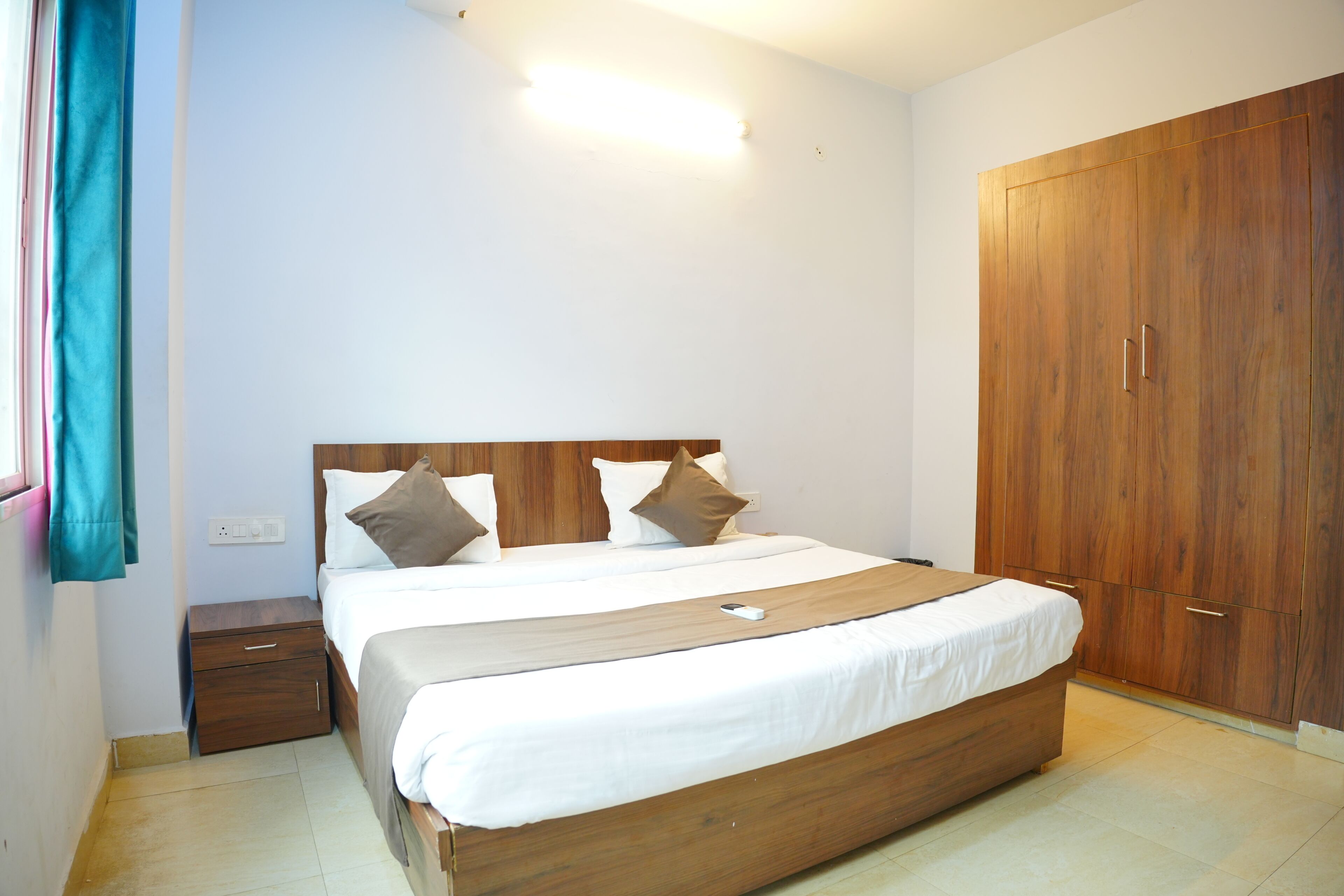 Quarto com cama de madeira, mesa de cabeceira, guarda-roupa e janela com cortinas.