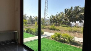 Quarto com uma janela grande, um sofá azul e vista para um gramado verde com palmeiras.