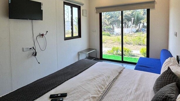 Quarto de hotel moderno com uma cama grande, um ventilador de teto, TV fixada na parede e uma janela com vista para o exterior.