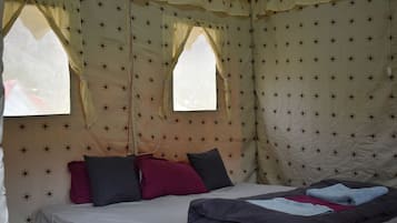 Uma cama com almofadas e um cobertor, uma janela com cortinas e uma parede estampada.