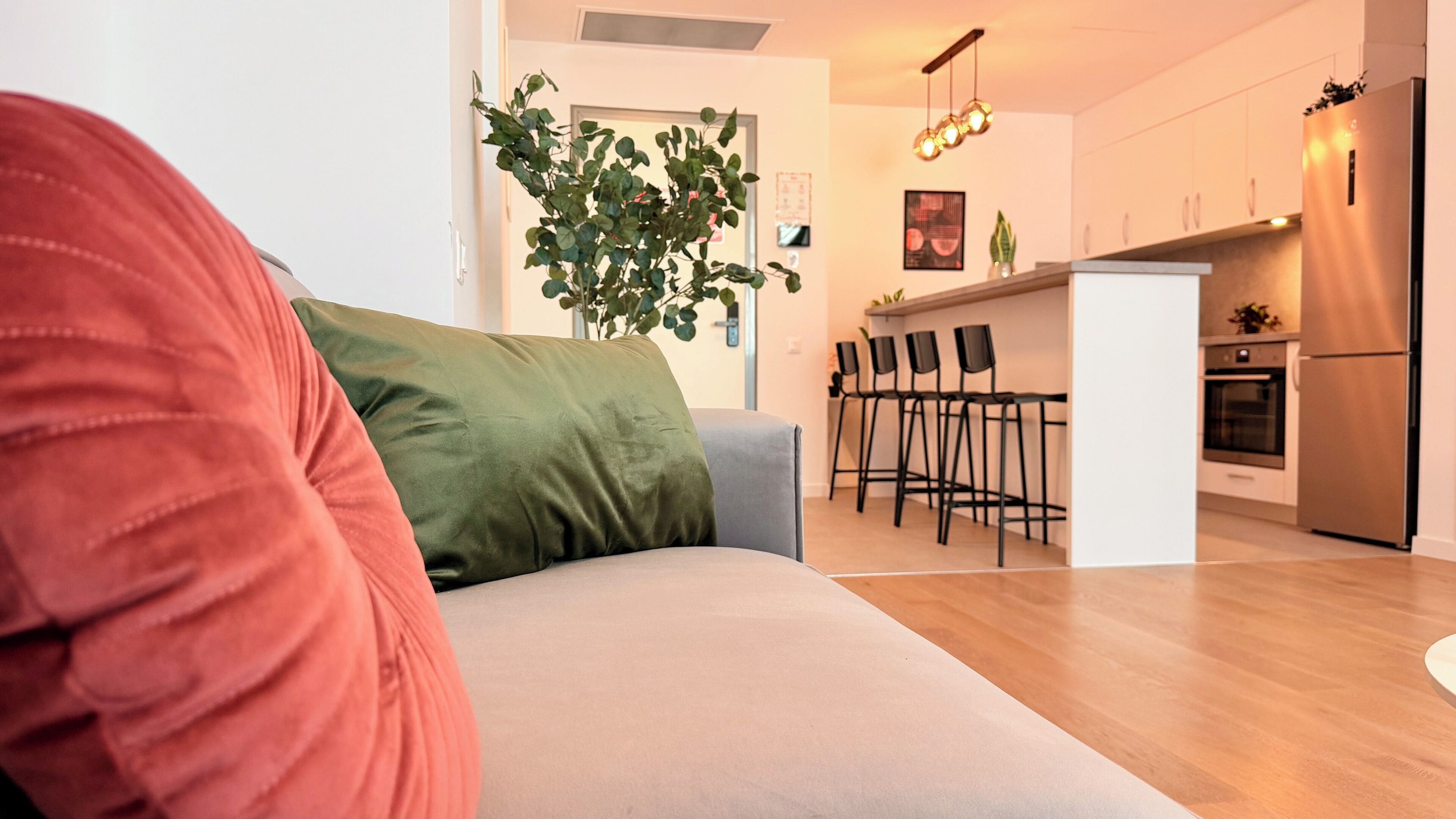 Uma sala de estar moderna com um sofá, uma área de jantar com cadeiras, uma cozinha com geladeira e uma planta em vaso.