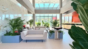 Um hall amplo com um sofá branco moderno, plantas em vasos e um balcão de recepção.