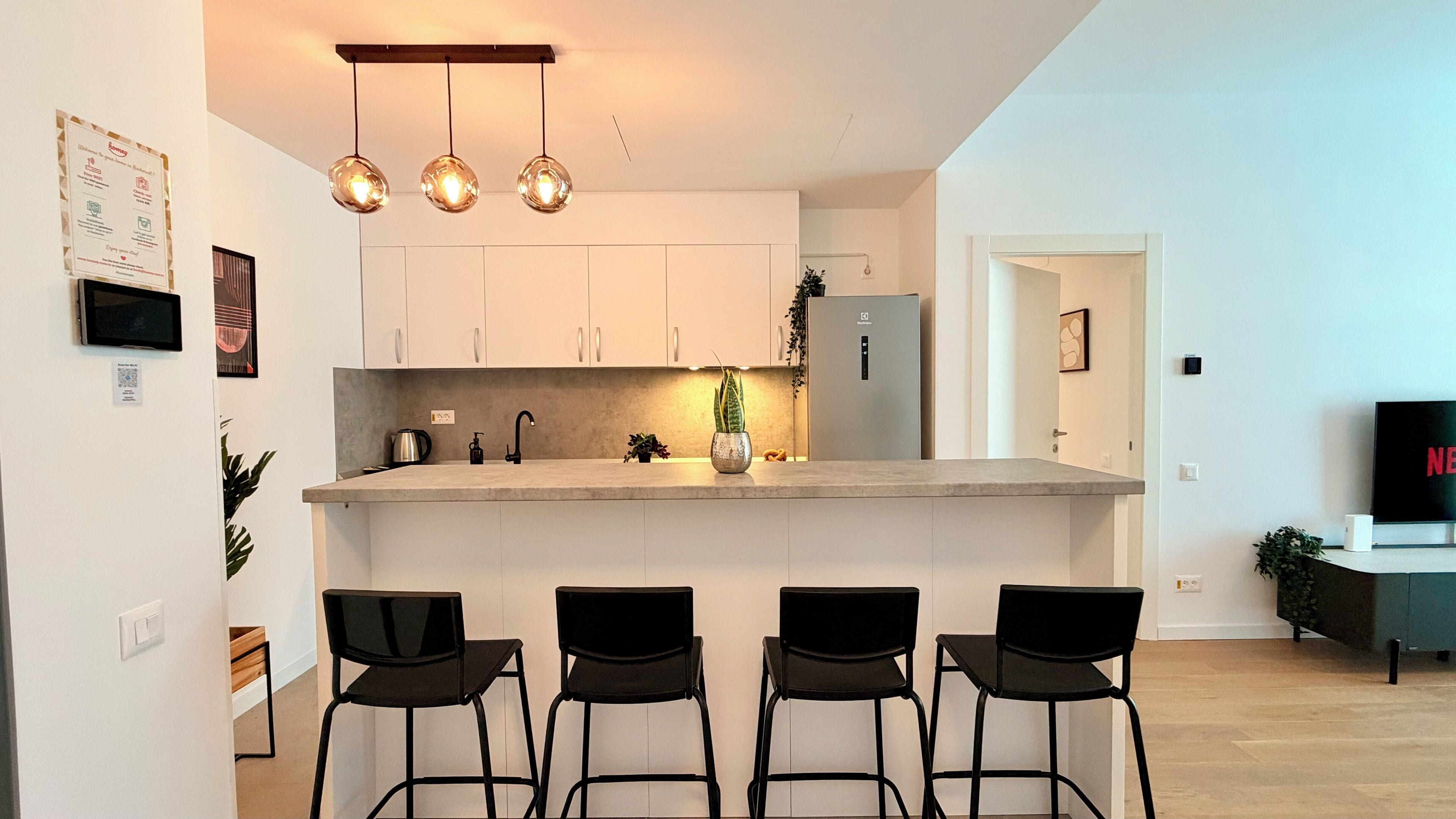 Uma cozinha moderna com armários brancos, uma ilha central com banquetas e iluminação pendente.