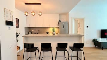 Uma cozinha moderna com armários brancos, uma ilha central com banquetas e iluminação pendente.