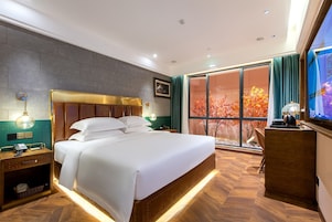 Quarto de hotel com uma cama grande, uma escrivaninha com telefone e vista para folhas de outono pela janela.