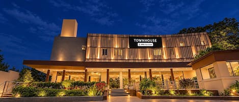 Uma casa geminada moderna com uma placa chamativa 'TOWNHOUSE', entrada bem iluminada e um jardim ajardinado.