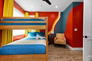 Uma cama beliche com roupa de cama azul, uma cadeira e uma parede com um design abstrato e colorido.