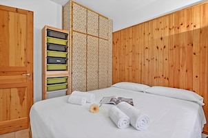 Quarto de hotel com guarda-roupa de madeira, cama com roupa de cama branca e painel de parede de madeira.