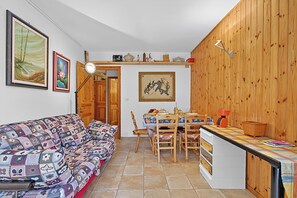 Uma sala de estar aconchegante com um sofá, uma mesa de jantar com cadeiras e uma área de cozinha com uma parede de madeira e um lustre.