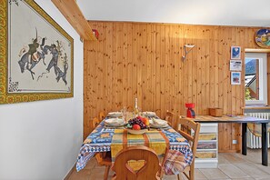Uma sala de jantar com parede de madeira, uma mesa posta para quatro pessoas e uma janela com vista para montanhas.