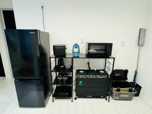 Uma cozinha compacta equipada com geladeira, micro-ondas, cafeteira, prateleira pequena com chaleira e copos.