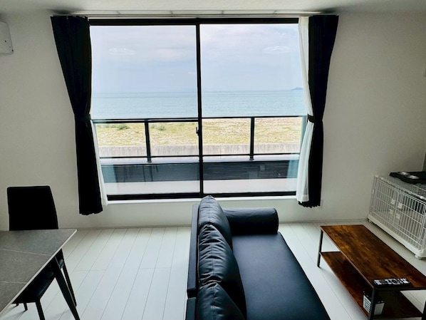Quarto com uma janela grande, um sofá, uma mesa e uma mesinha de madeira.