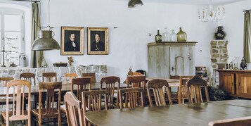 Uma sala de jantar com cadeiras de madeira e uma mesa, uma parede de pedra e um candelabro.