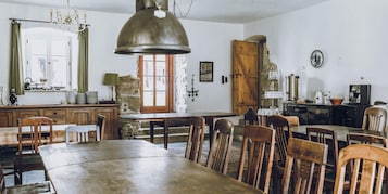 Uma sala de jantar tradicional com uma grande mesa de madeira, várias cadeiras, um candelabro e uma porta de madeira rústica.