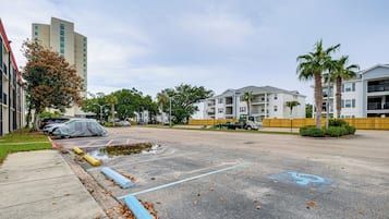 Um estacionamento com um carro coberto, um edifício com vários andares e um céu claro.