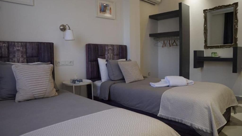 Quarto de hotel com duas camas, uma mesa de cabeceira, um abajur, um espelho e uma prateleira com objetos.