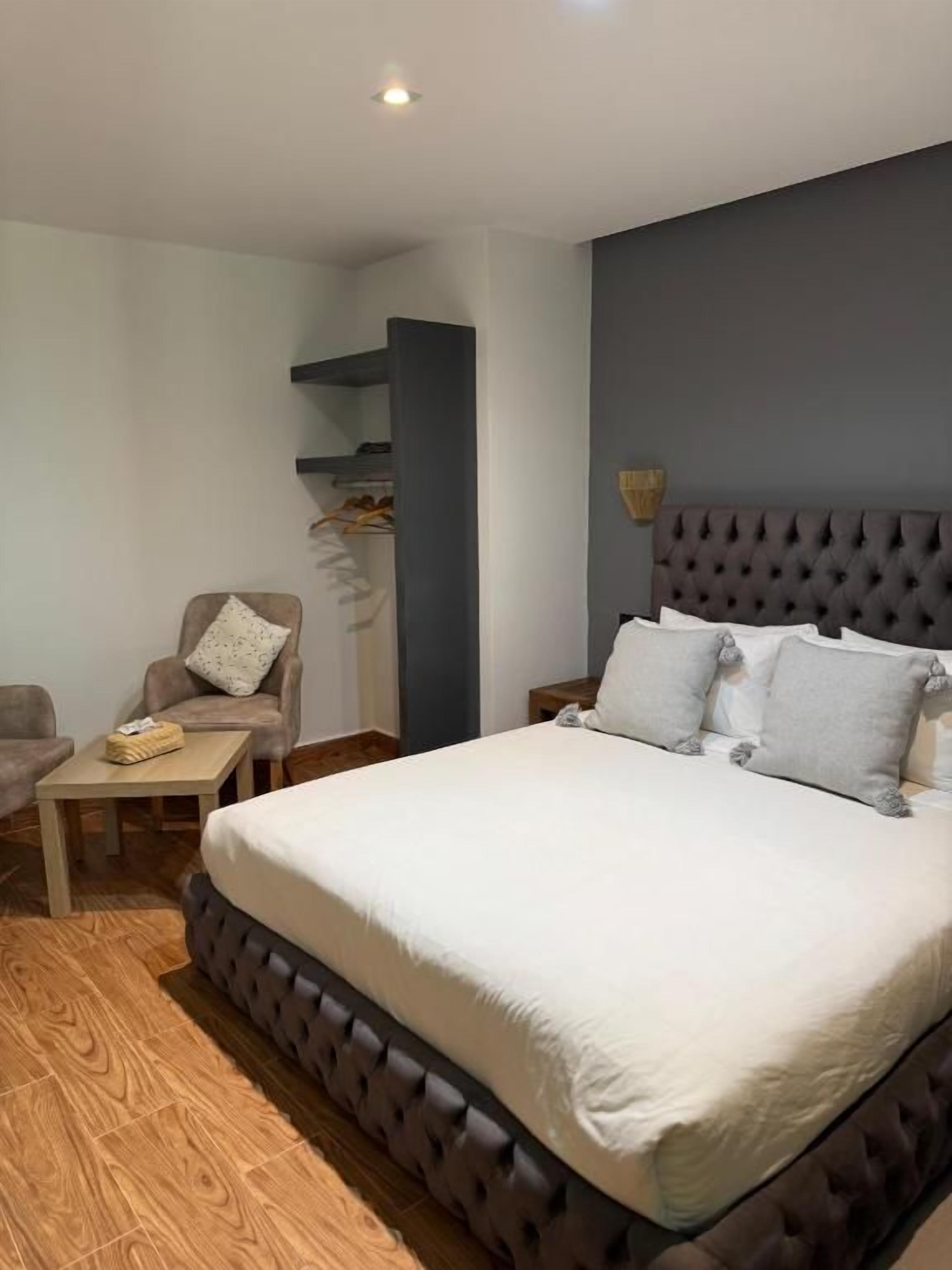 Quarto com uma cama grande, uma cadeira, uma mesinha e um guarda-roupa.