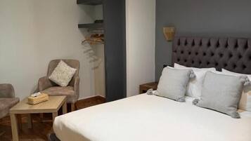 Quarto com uma cama grande, uma cadeira, uma mesinha e um guarda-roupa.