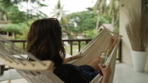 Uma pessoa relaxando em uma rede ao ar livre, segurando uma bebida.