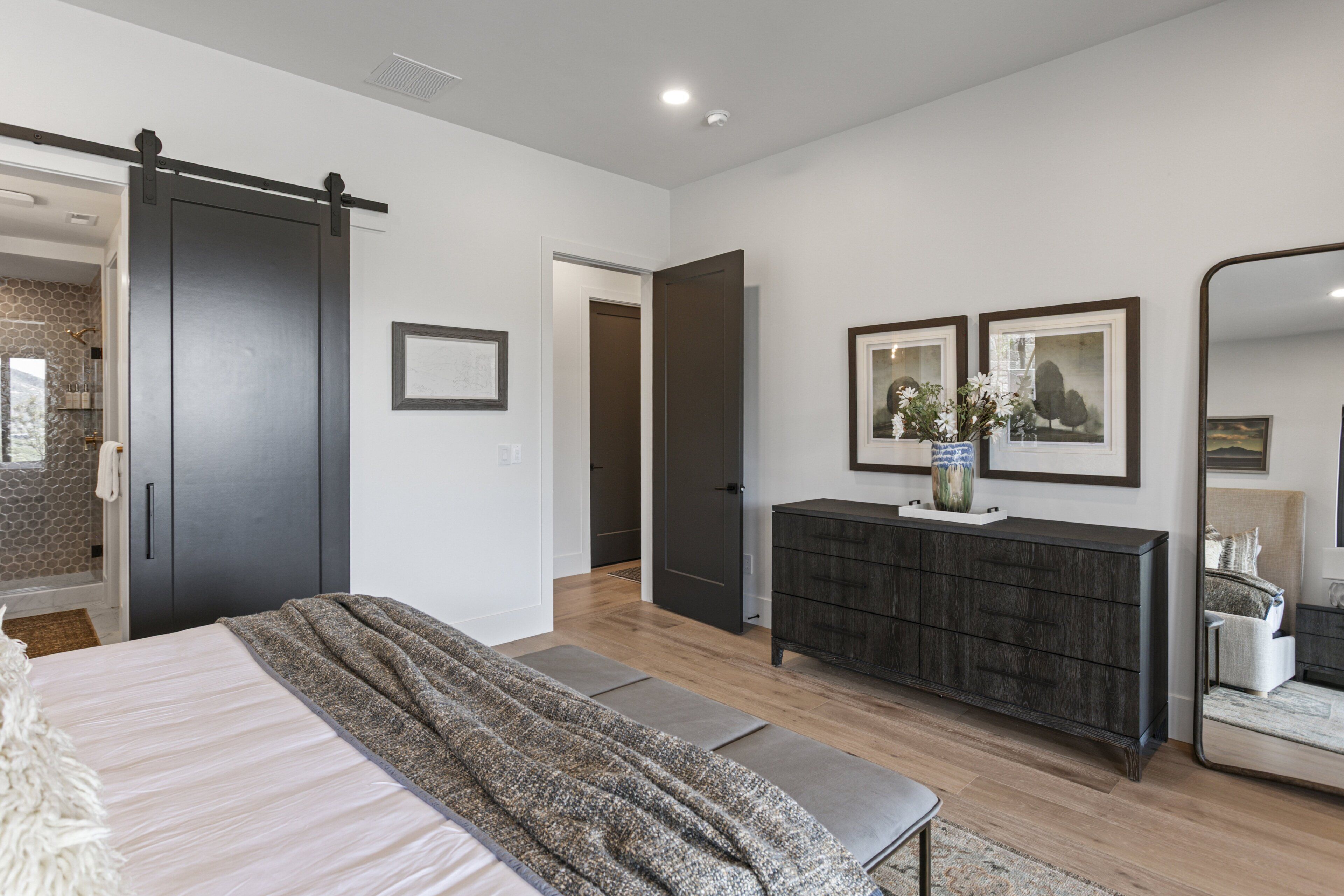 Quarto com uma cama, cômoda, espelho e porta que dá para outro ambiente.