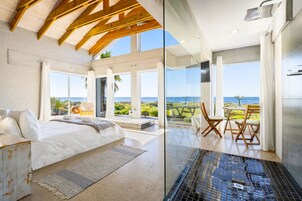 Um quarto moderno com uma cama grande, vista para o mar e um banheiro envidraçado com banheira.