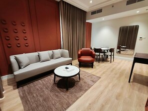 Uma sala de estar moderna com um sofá, uma poltrona vermelha, uma mesa de centro redonda e uma área de jantar com mesa e cadeiras.