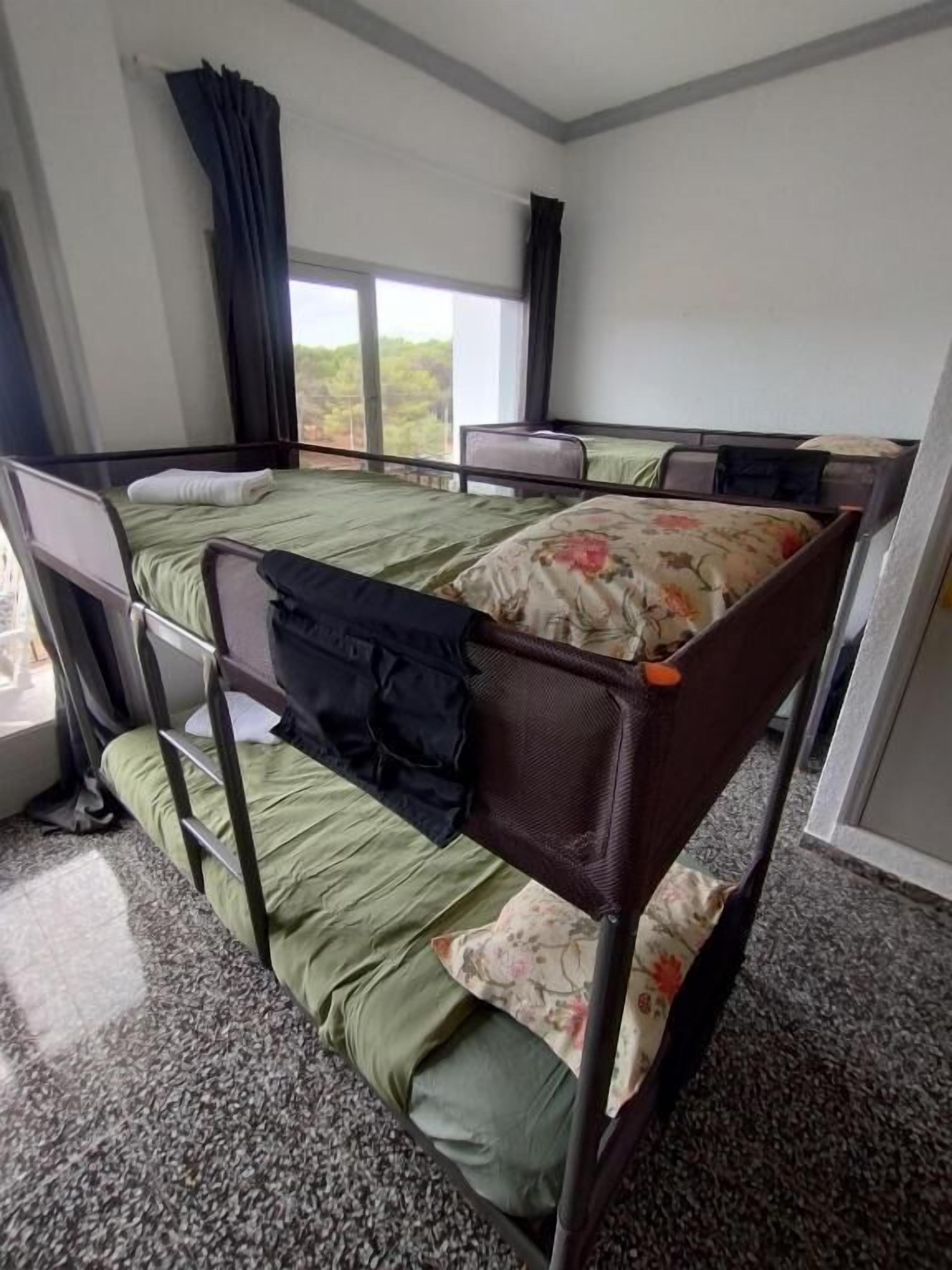 Um quarto com beliches, uma janela com cortinas e piso coberto de carpete.