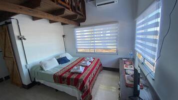 Quarto com cama, janela com persianas, escrivaninha com computador e ventilador de teto.