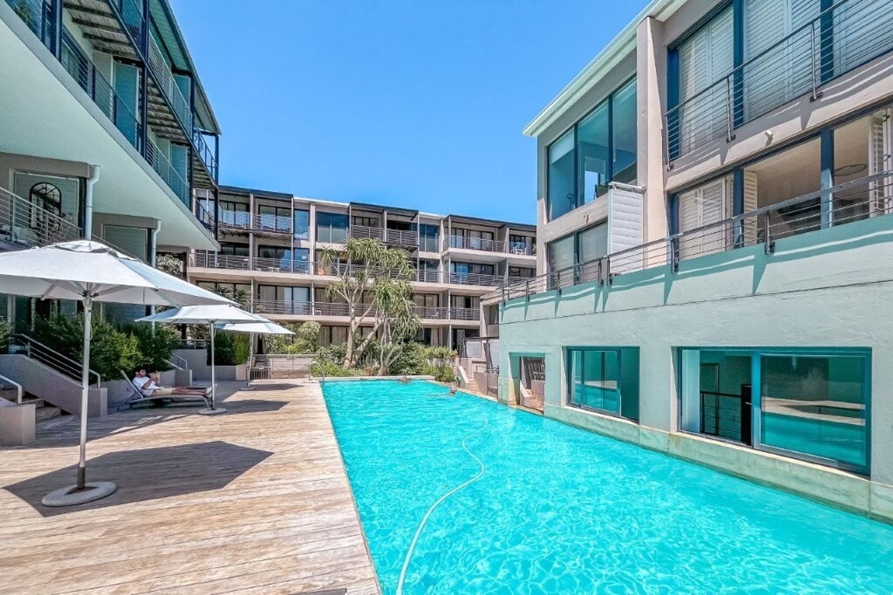 Área de piscina com deck de madeira, espreguiçadeiras e guarda-sóis.