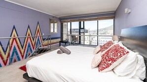 Quarto de hotel com uma cama grande, vista para a cidade e uma decoração colorida na parede.