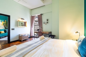 Quarto com cama, escrivaninha, cadeira, mesinha, espelho e janela com cortinas.