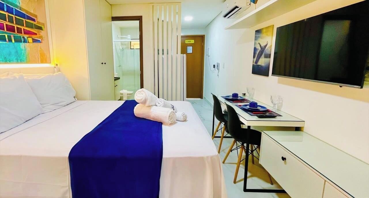 Quarto de hotel com cama, escrivaninha e televisão.