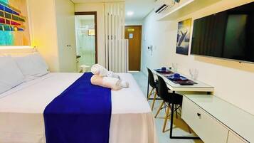 Quarto de hotel com cama, escrivaninha e televisão.