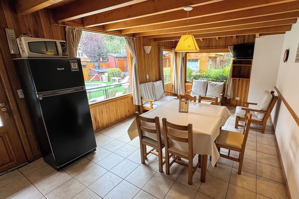 Área de refeições com mesa, cadeiras, geladeira e vista para o exterior.