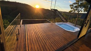 Um deck de madeira com uma banheira de hidromassagem e uma escadaria que dá acesso a um nível superior.