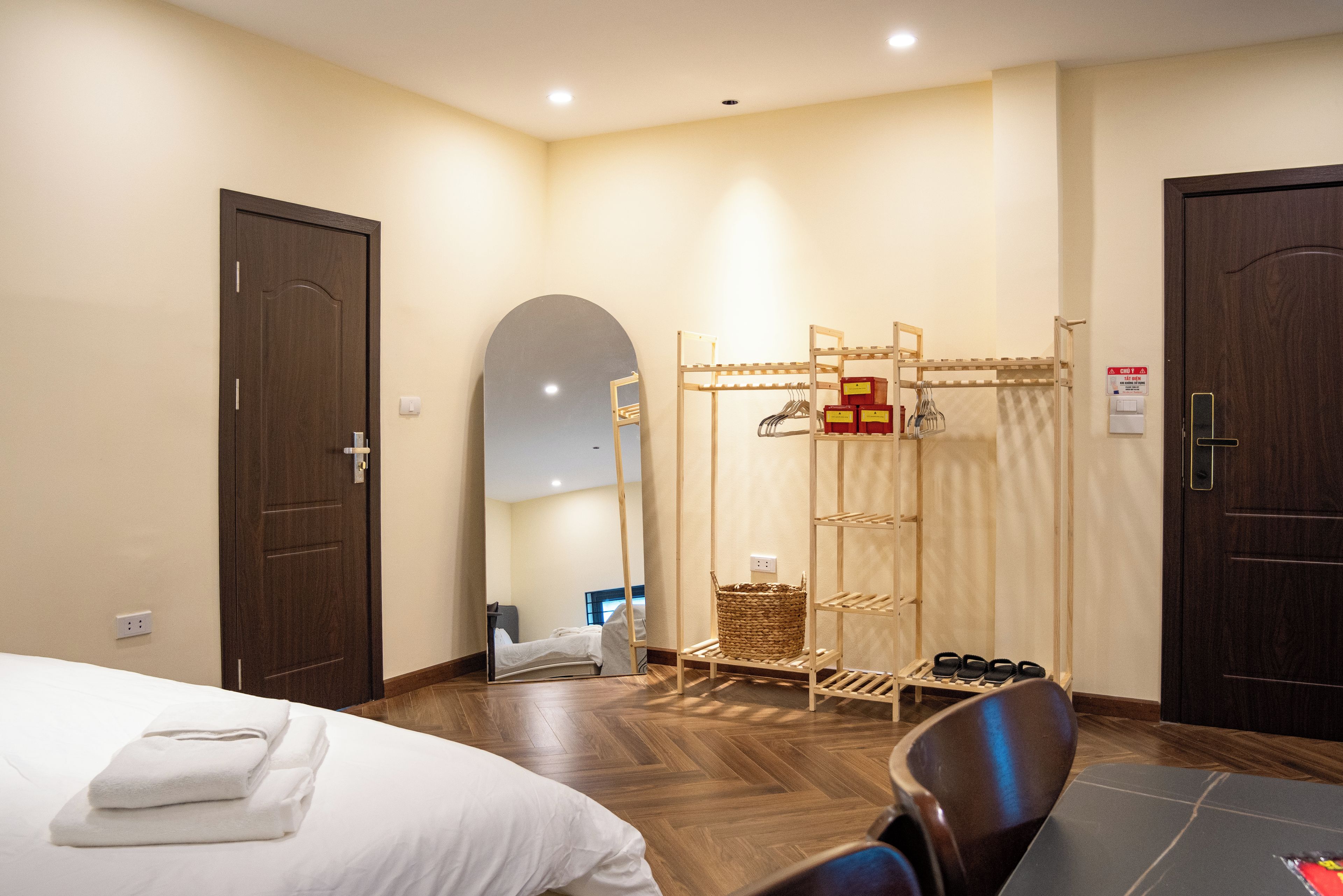 Quarto de hotel com cama, área de estar, espelho e suporte de madeira com caixas de armazenamento.