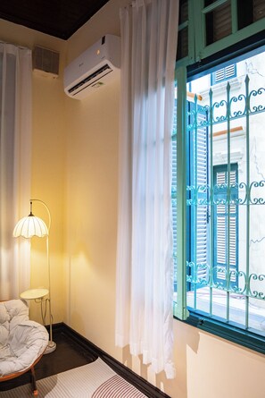 Quarto com cama, mesa de cabeceira, luminária, janela com grades de ferro decorativas e ar condicionado.