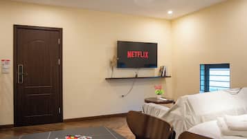Quarto de hotel com cama, televisão na parede, uma mesinha com lanches e uma porta.