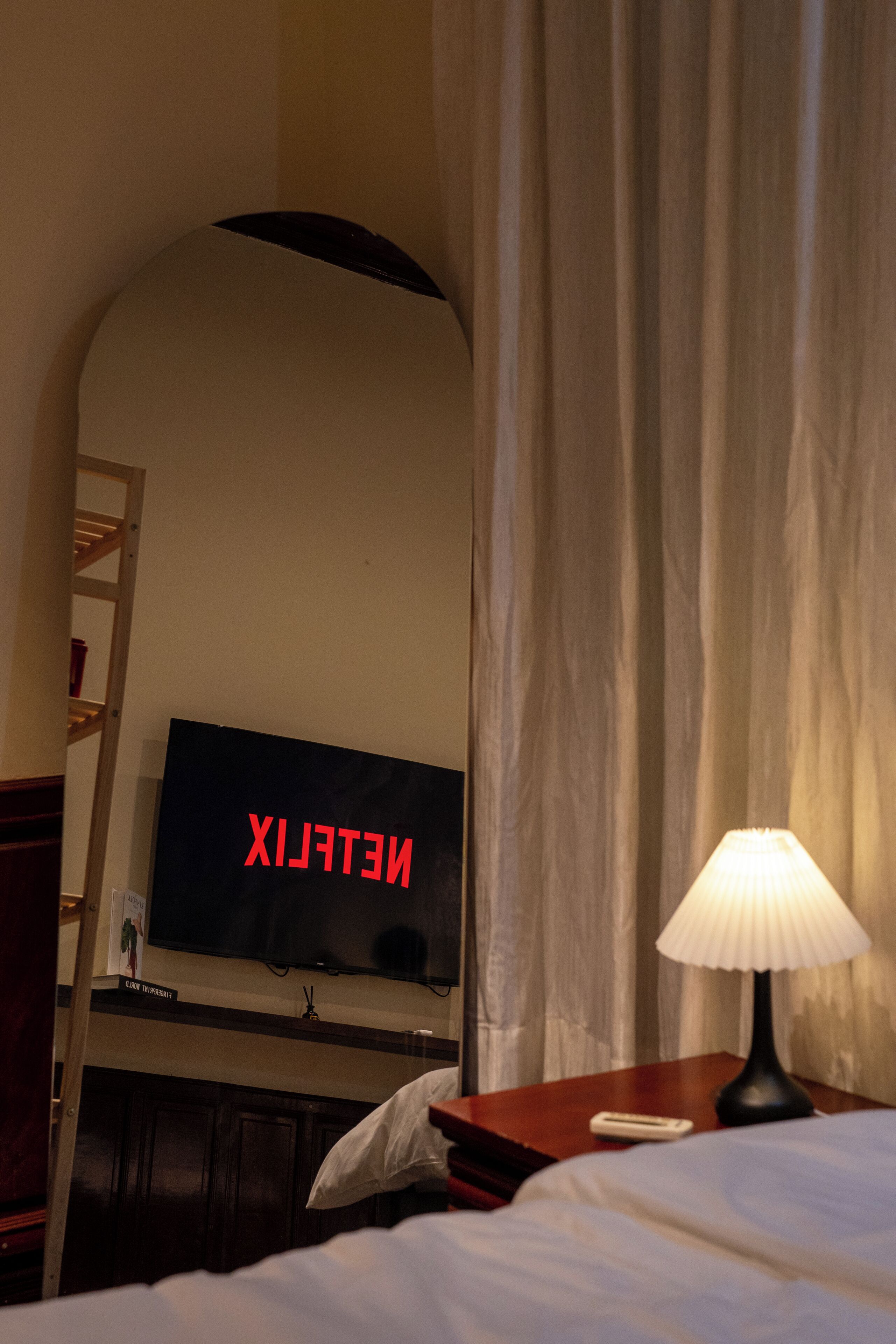 Quarto de hotel com cama, mesa de cabeceira com abajur, televisão na parede e cortina.