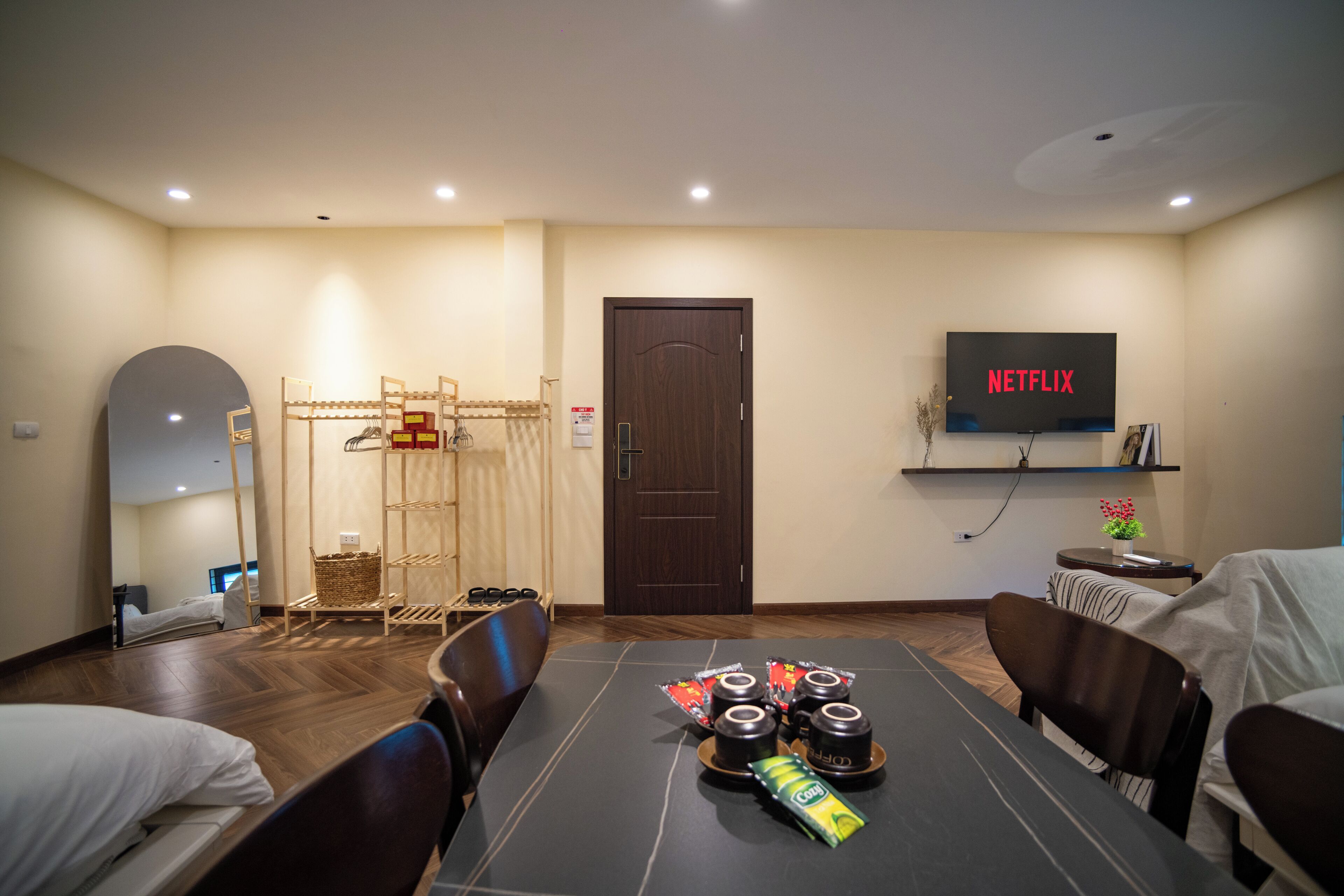 Quarto de hotel com mesa de jantar posta para dois, televisão fixada na parede e porta com moldura de madeira.