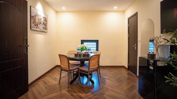 Uma sala de jantar com mesa redonda, quatro cadeiras, um vaso com flores e uma televisão.