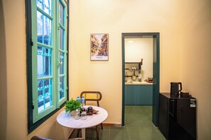Um corredor estreito com área de refeições, incluindo uma mesa redonda, cadeiras e um vaso de planta. Uma moldura com fotografia de Hanói está na parede.