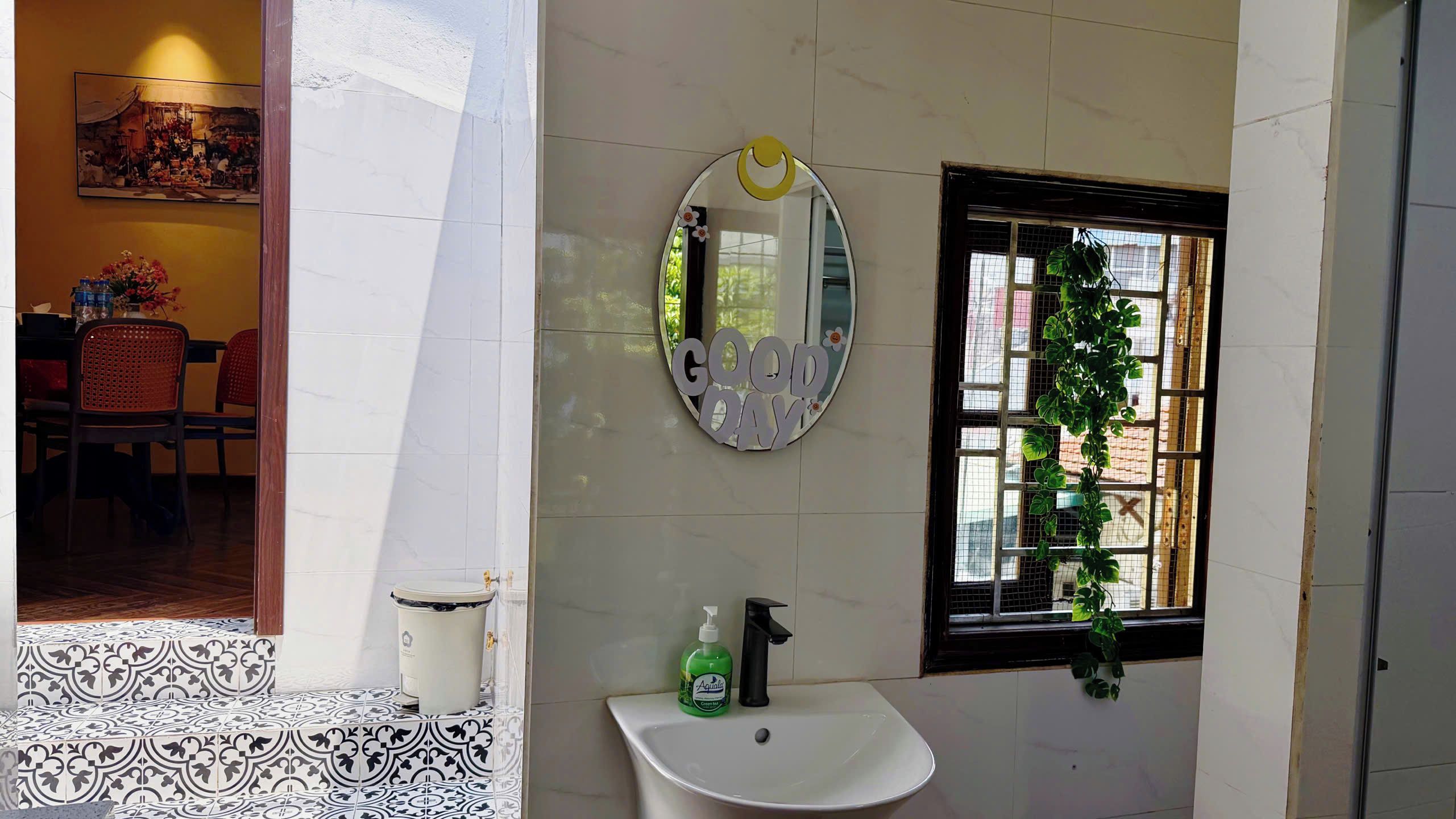 Casa de banho com uma pia branca, espelho e janela com plantas.