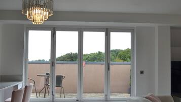 Uma sala de estar moderna com um sofá branco, um espaço de refeições com cadeiras, um candelabro e uma vista para área externa por meio de portas deslizantes amplas.