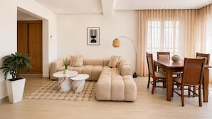Uma sala de estar moderna com um sofá modular, uma mesa de jantar com cadeiras, um abajur e um vaso de plantas.
