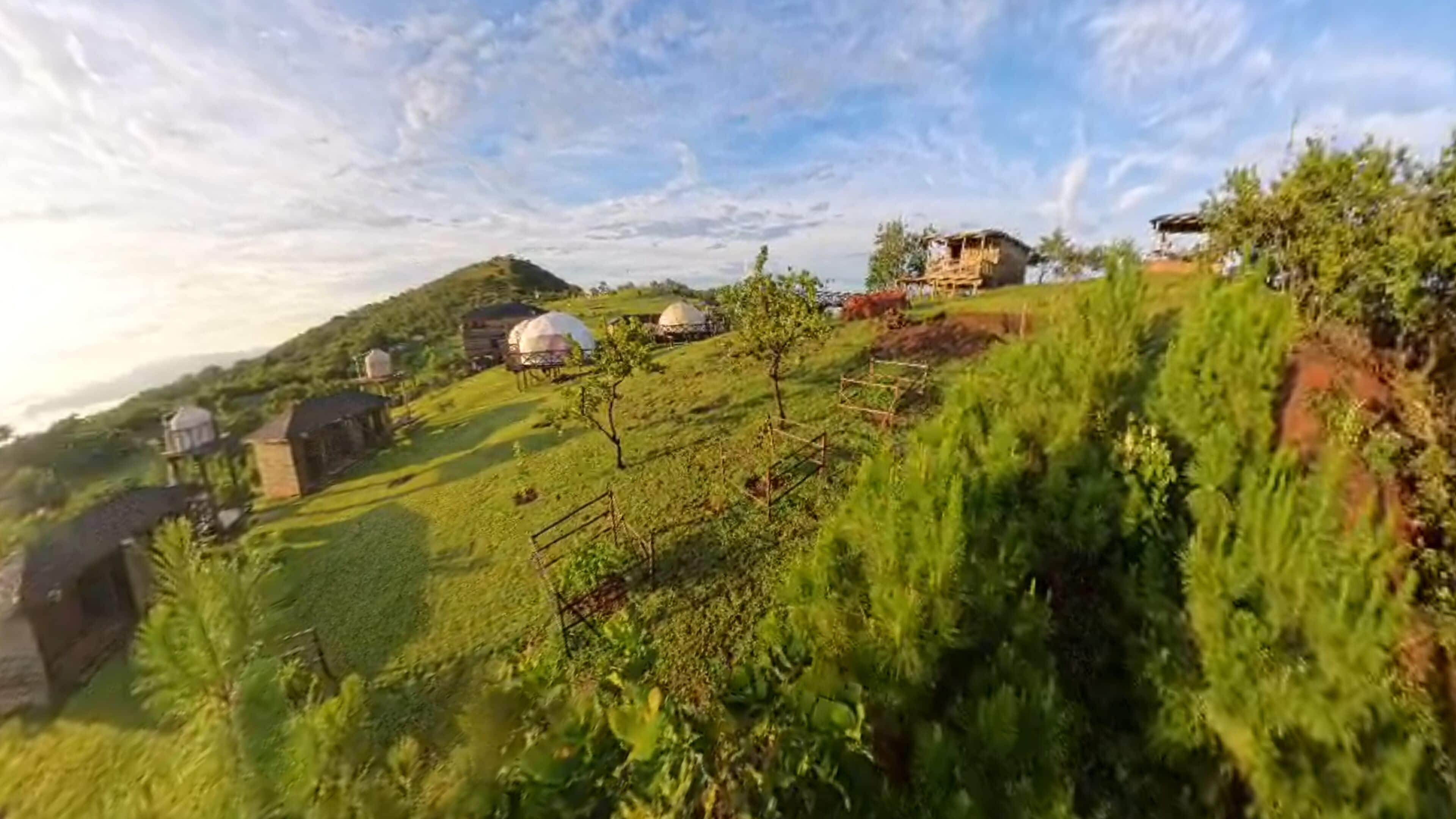 Paisagem rural com várias estruturas arredondadas, possivelmente iurtes, numa encosta.