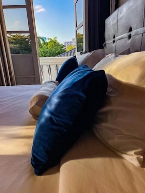 Cama com cabeceira, almofadas e vista para o verde lá fora.