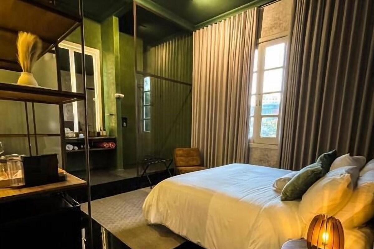 Quarto de hotel com cama, mesa de cabeceira, abajur e um espelho grande.