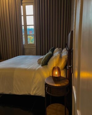 Um quarto com uma cama, uma luminária de cabeceira e uma janela com cortinas.