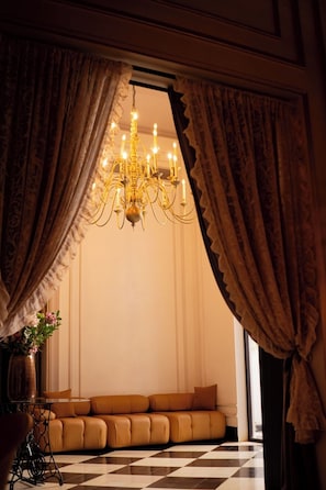Um quarto com um lustre grande e trabalhado, um sofá e cortinas.
